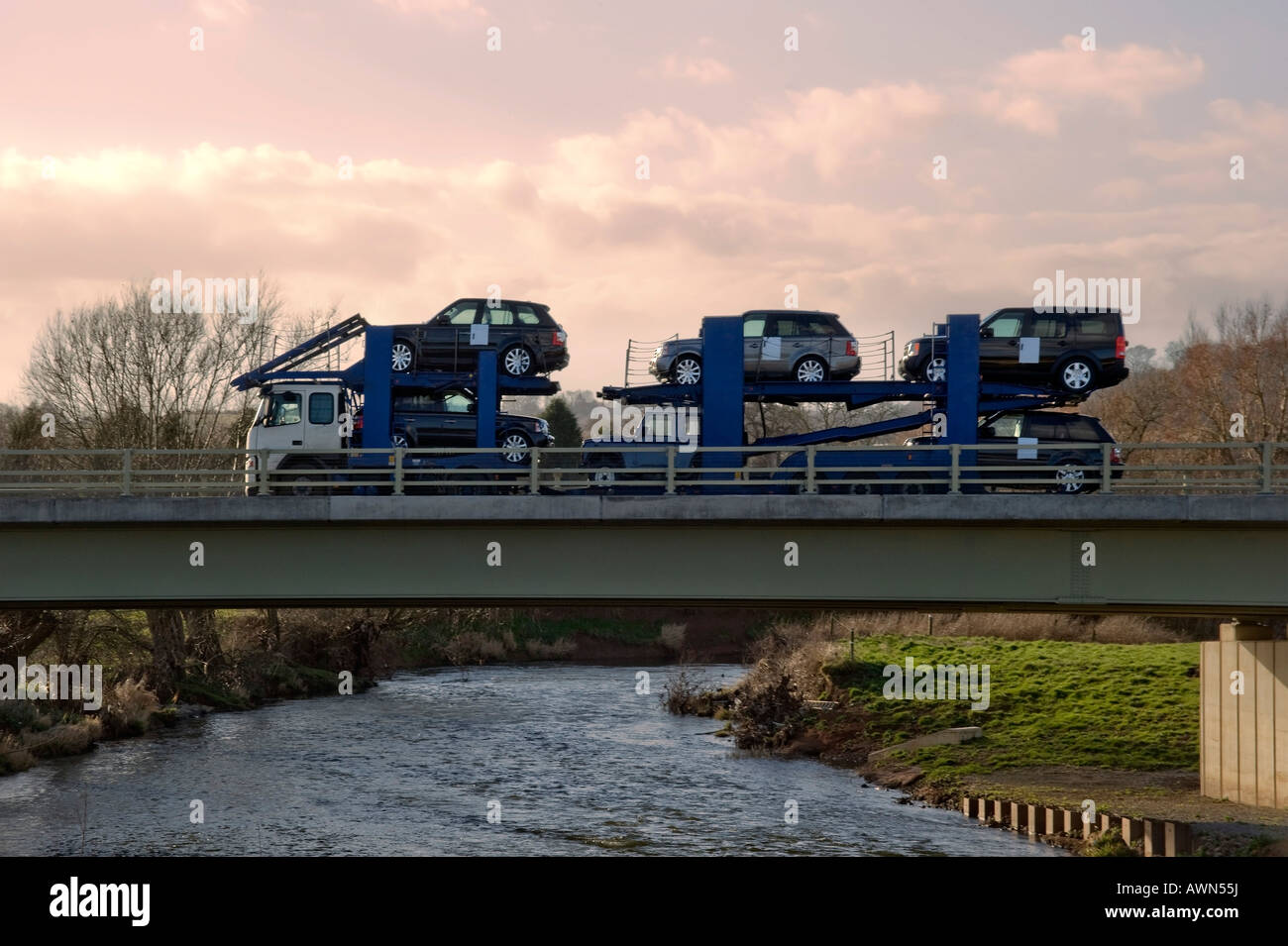 A car transporter carrying range rovers crossing a bridge over a river ...