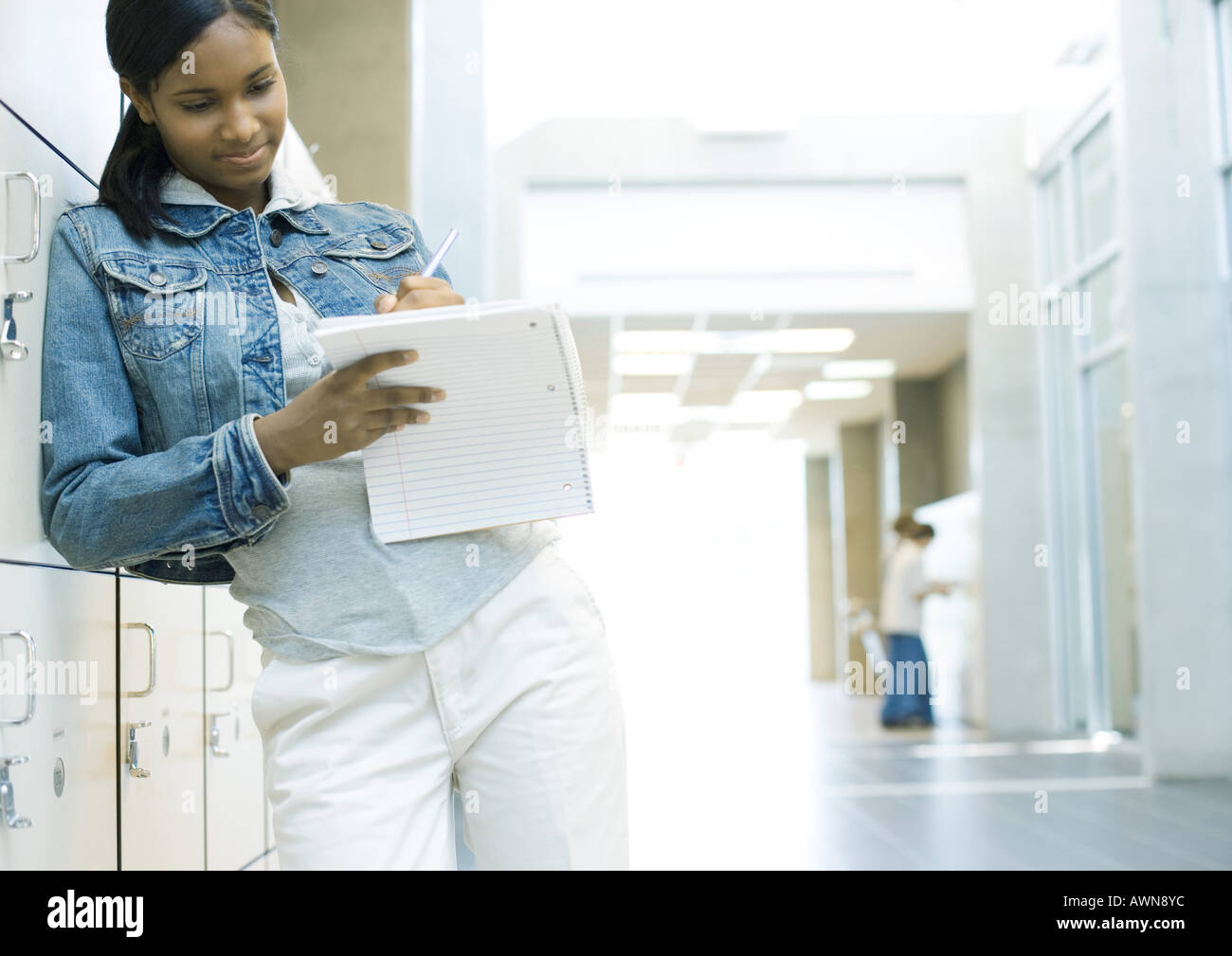 Teen girl standing by locker, writing in notebook Stock Photo - Alamy