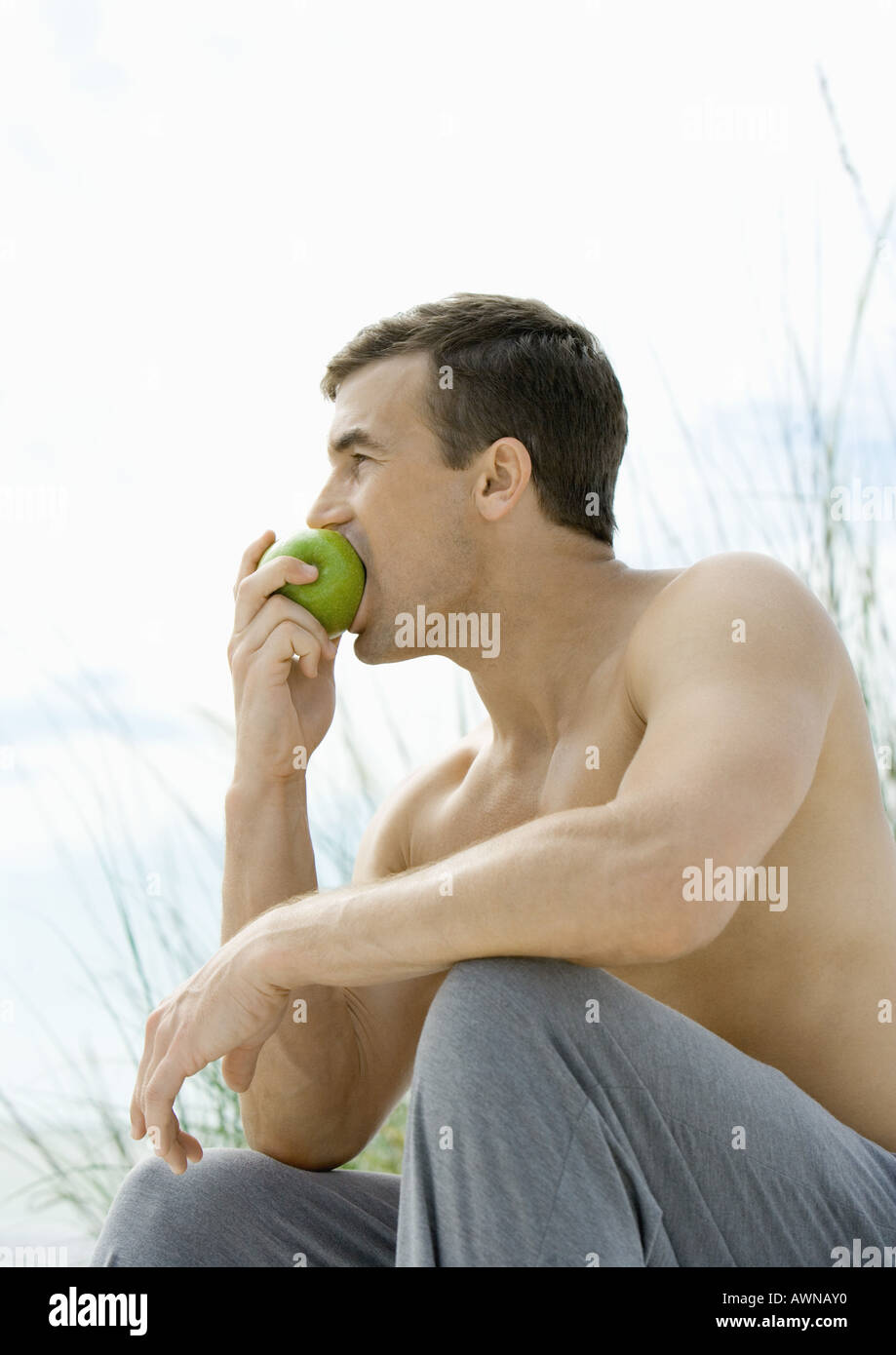Barechested man eating apple, side view Stock Photo - Alamy