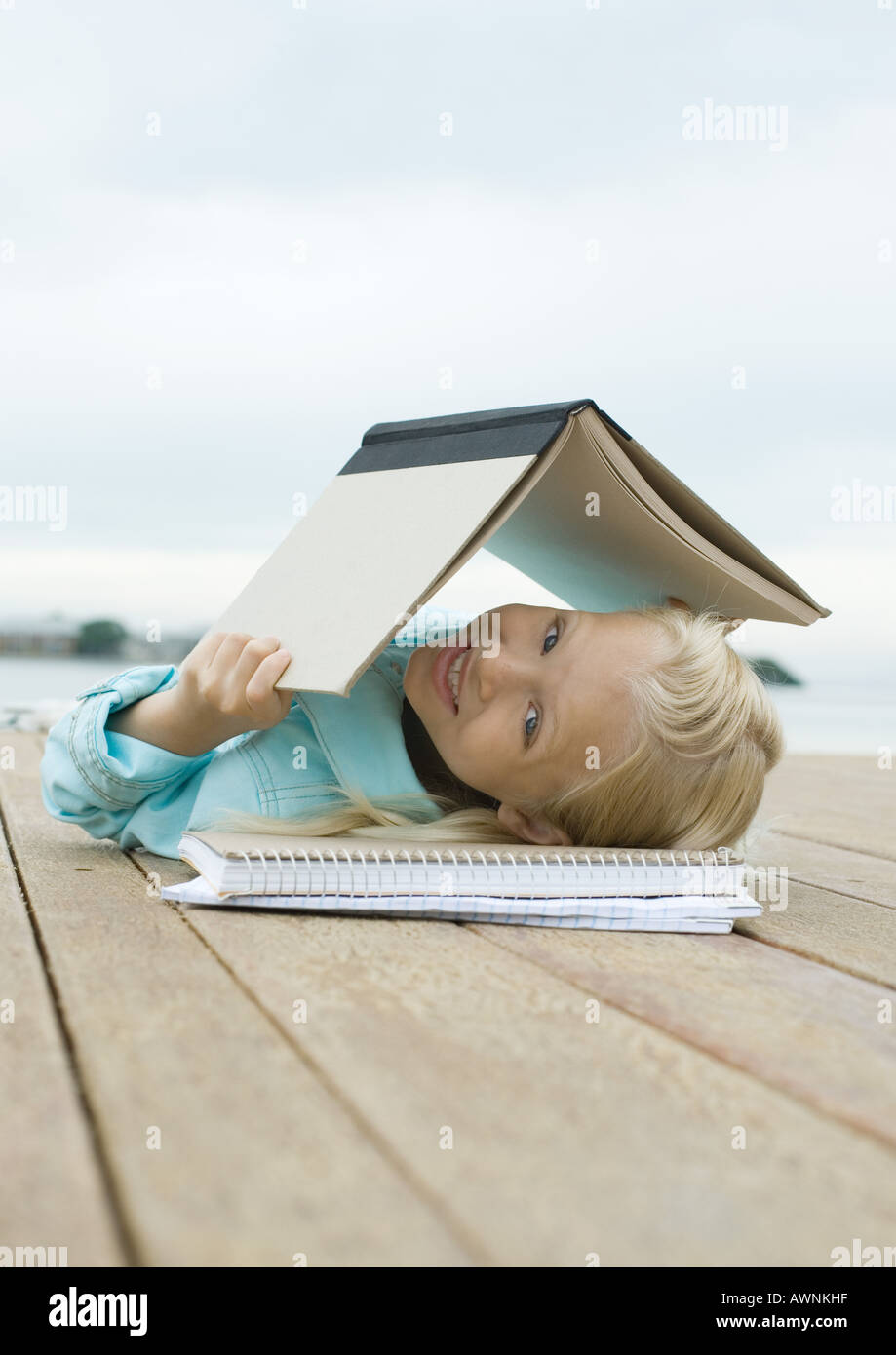 Girl lying on dock with book over head Stock Photo - Alamy