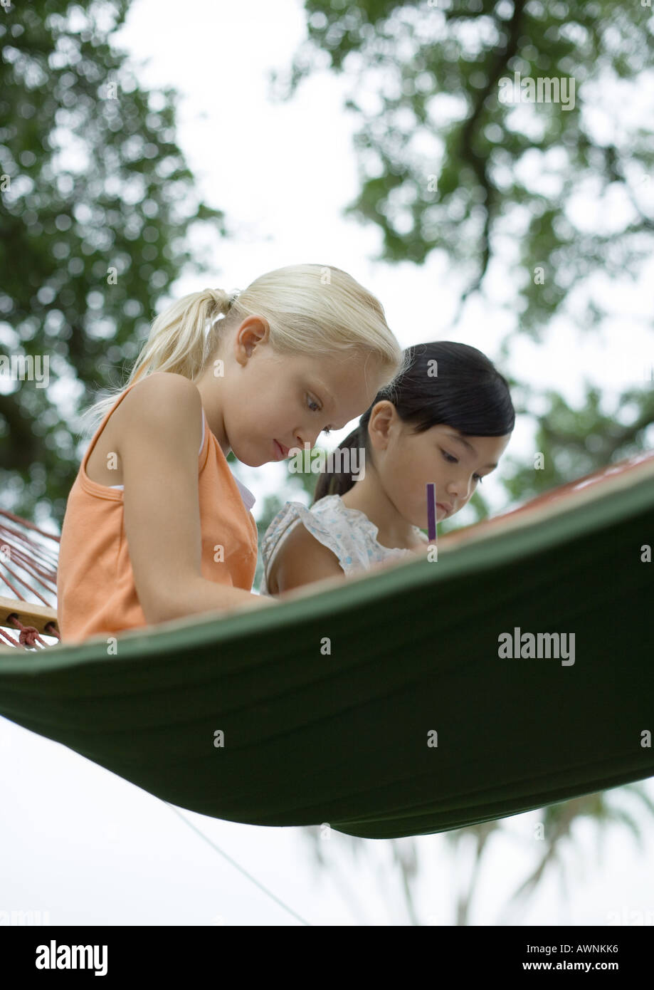 Two girls sitting in hammock, writing Stock Photo - Alamy