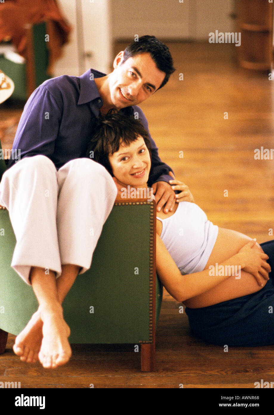 Man sitting backwards on chair and pregnant woman sitting on floor ...