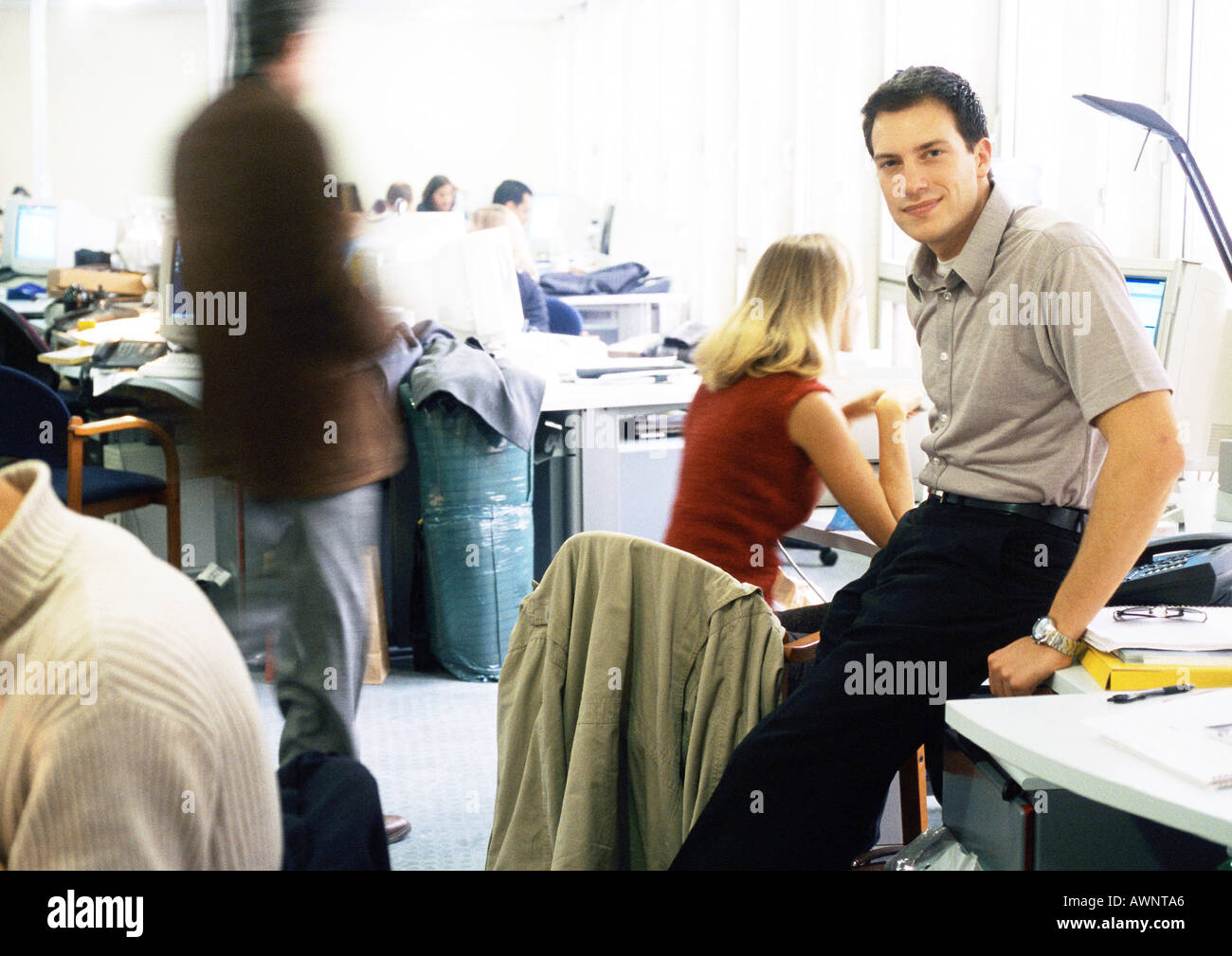 Man sitting on desk in office, looking at camera Stock Photo - Alamy