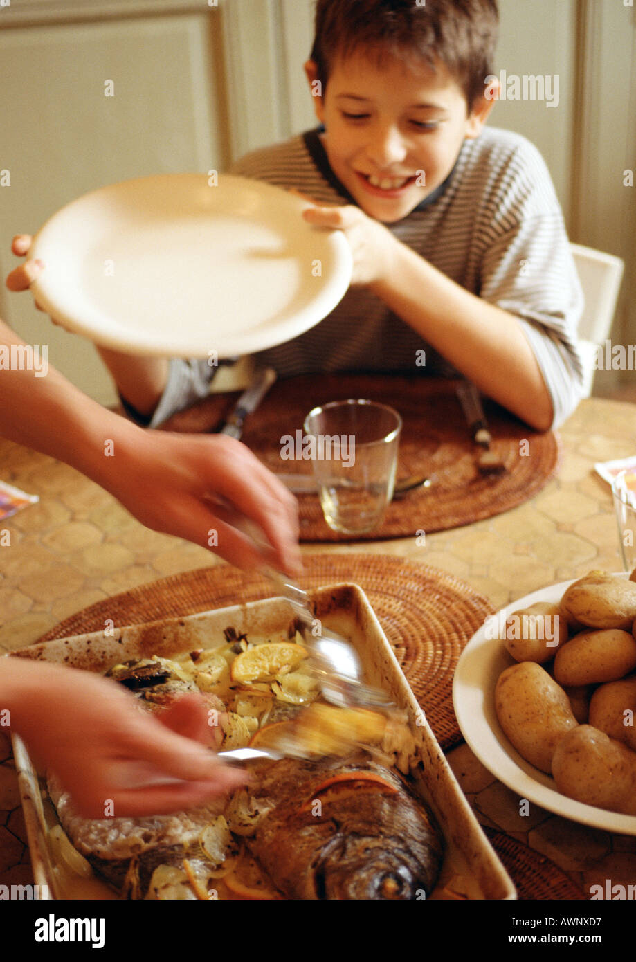 Child at table, holding plate, mother's hands serving food Stock Photo ...
