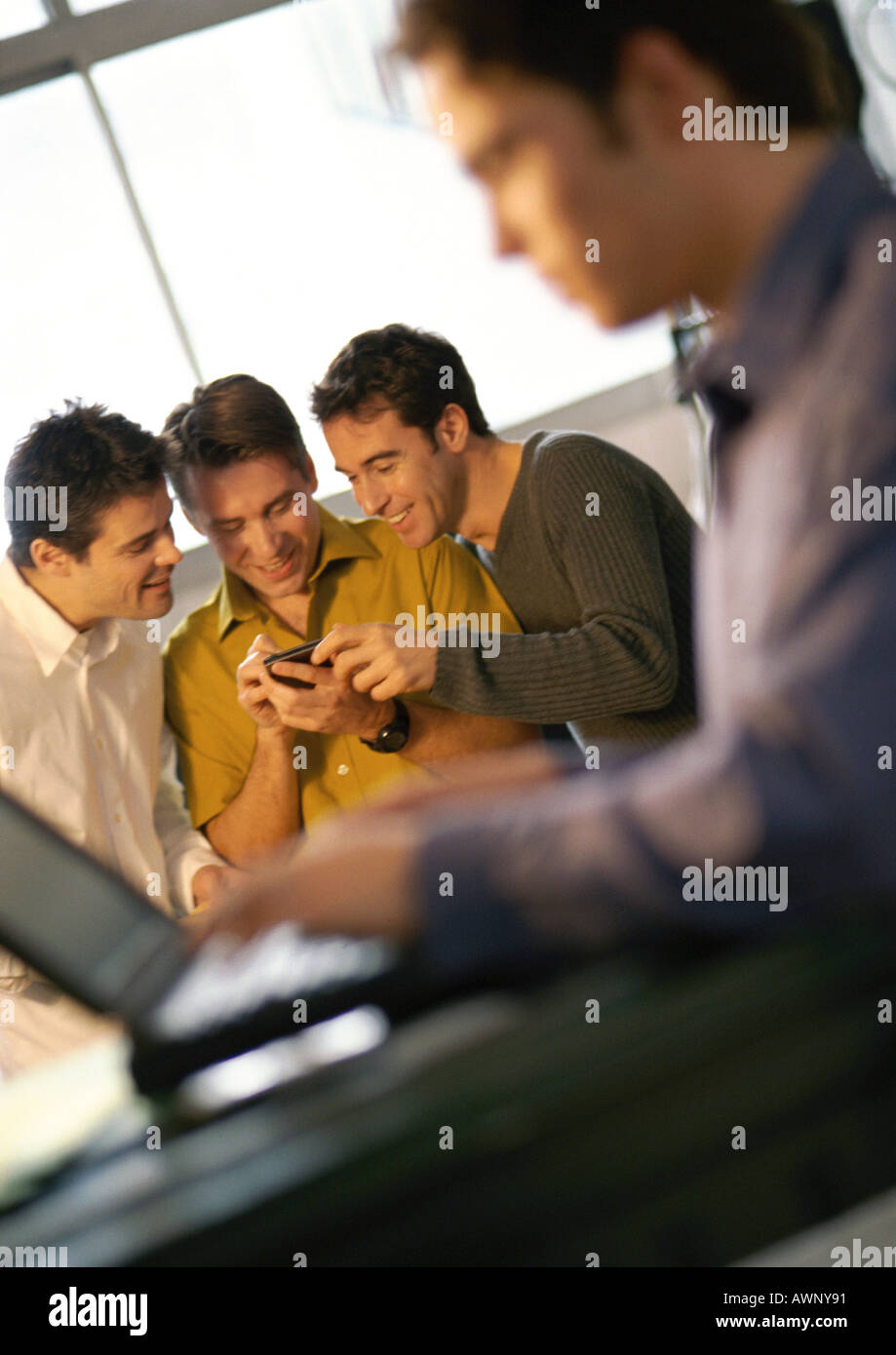 Three men looking at hand held computer, fourth man using laptop in ...