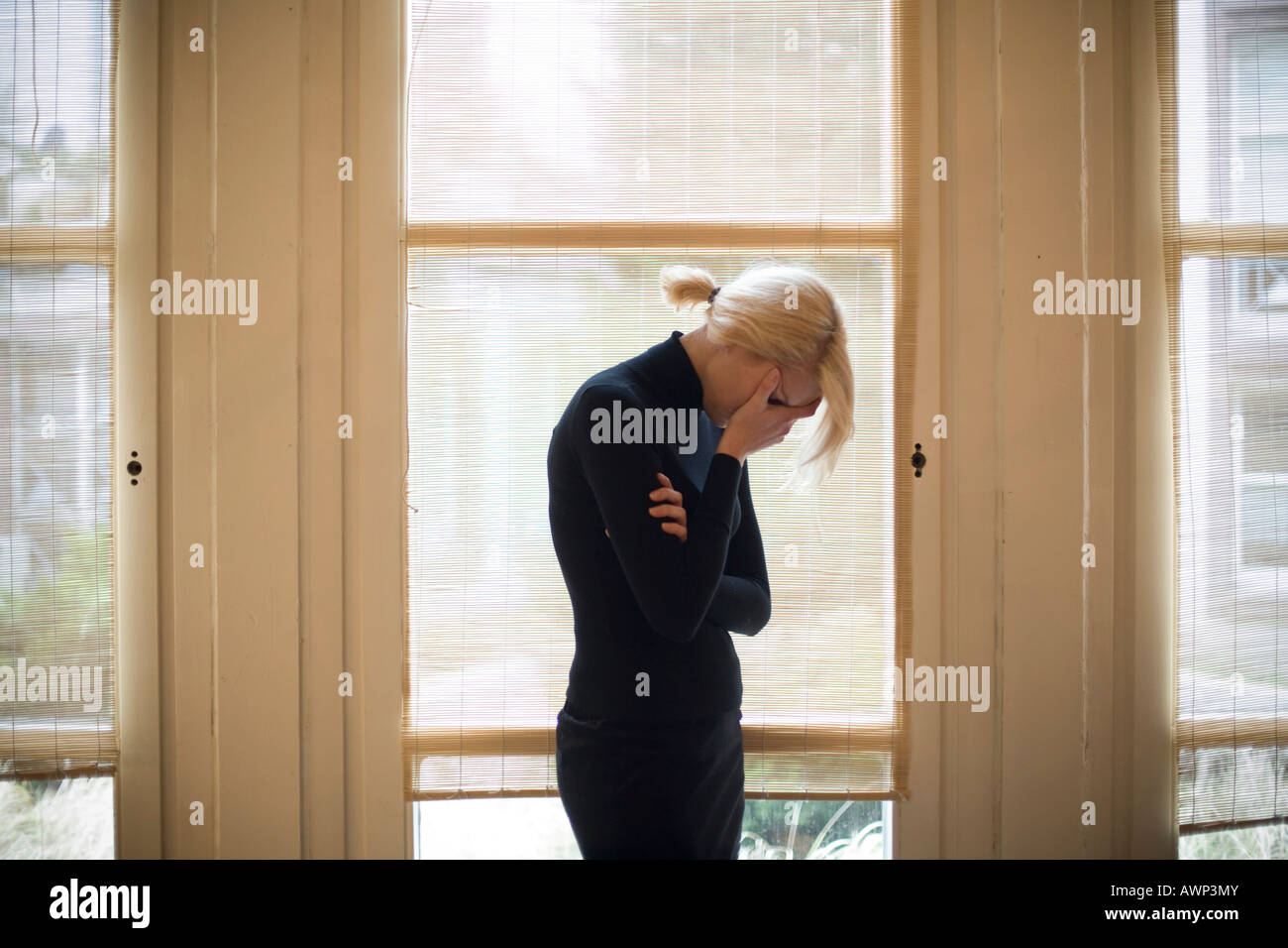 Sad blonde woman standing in front of large windows Stock Photo - Alamy