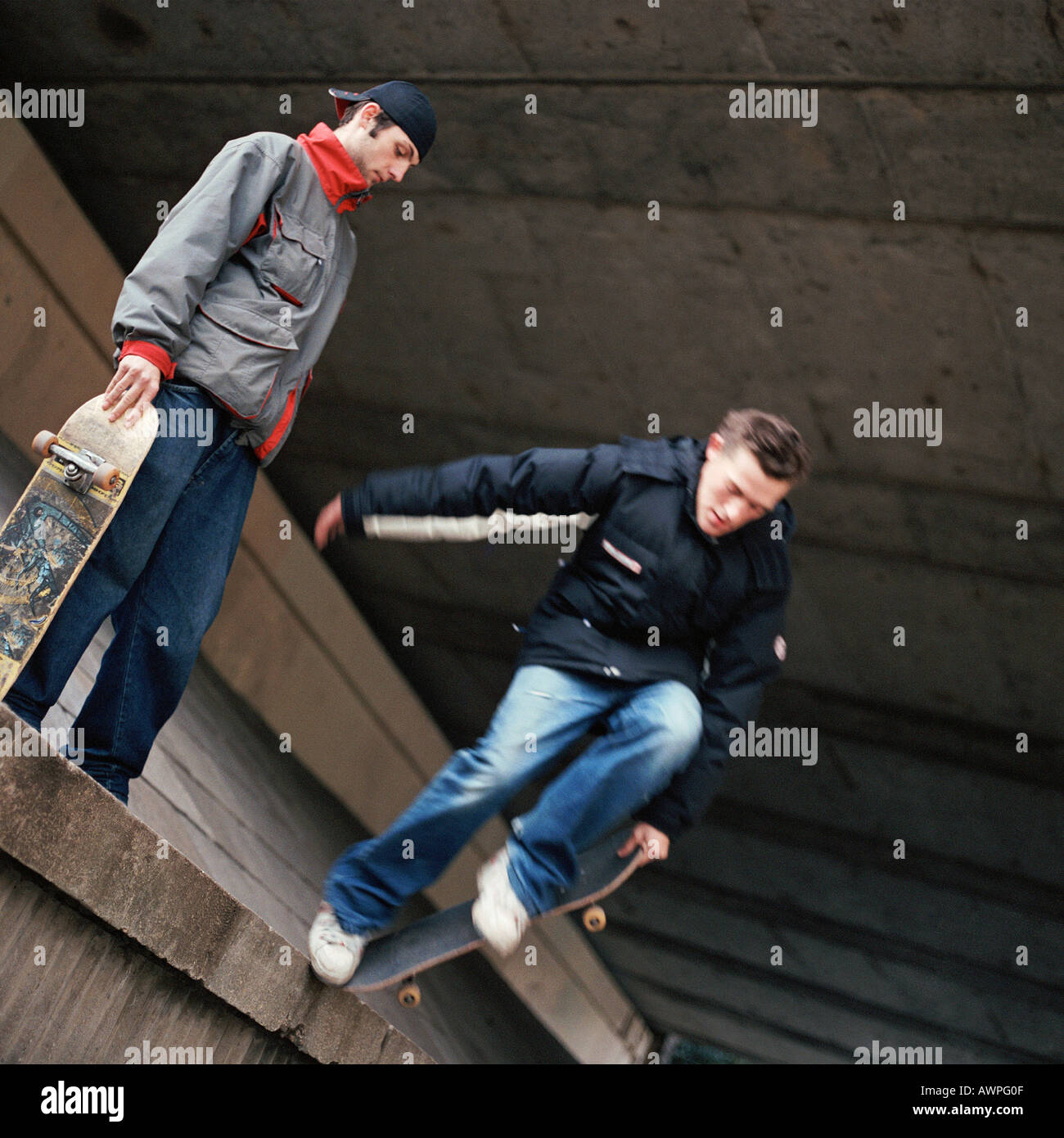 Two teenagers with skateboards, one jumping down from a wall Stock ...