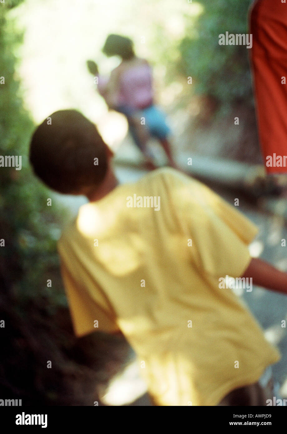 Child walking on path behind woman holding baby, rear view, blurred ...