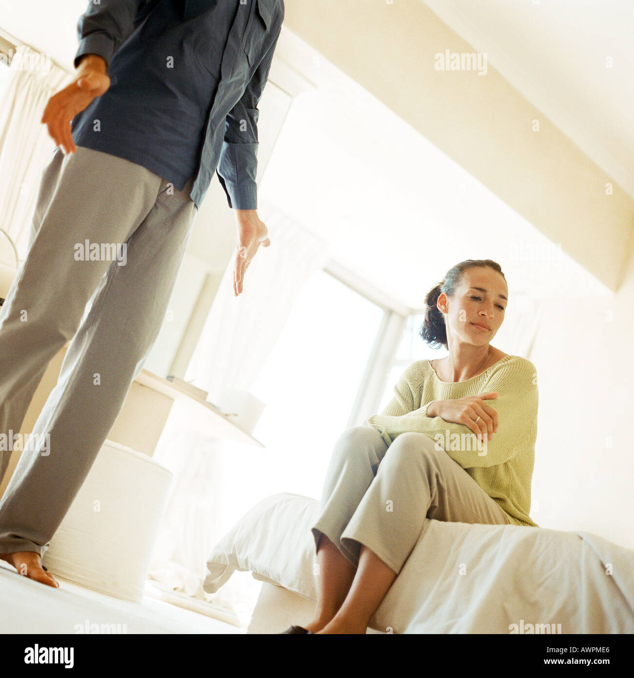 Man standing with hands out, beside woman sitting on bed and looking ...