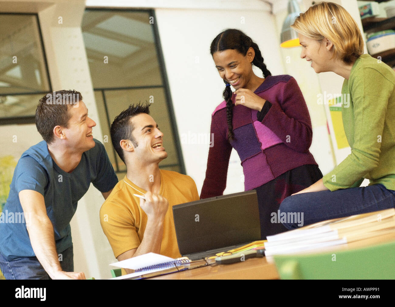 Four people smiling around desk with laptop computer Stock Photo - Alamy