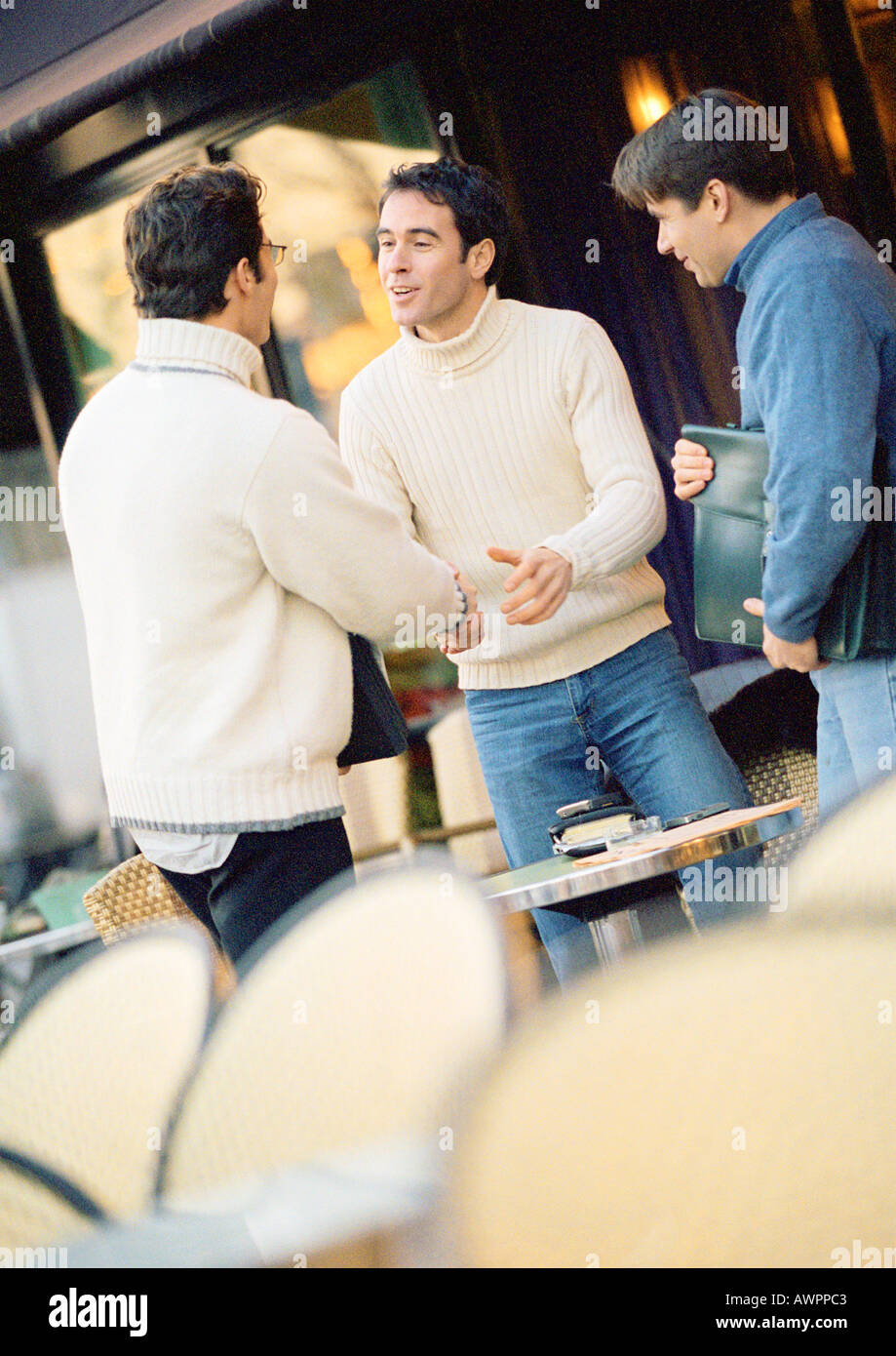 Three men at cafe terrace, two shaking hands Stock Photo - Alamy
