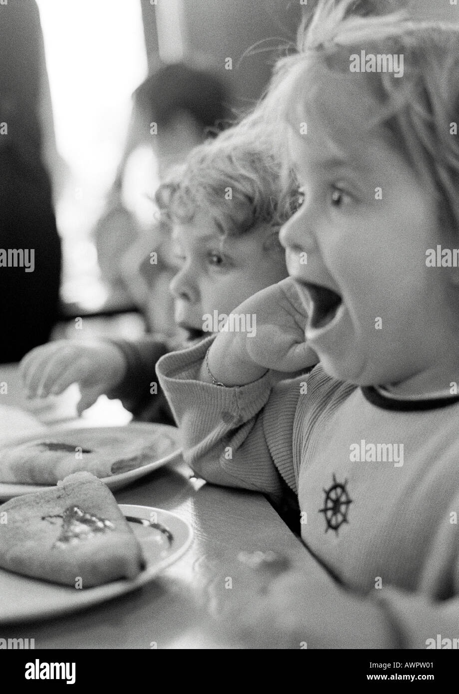 Children sitting at table, mouths open, side view, b&w Stock Photo - Alamy