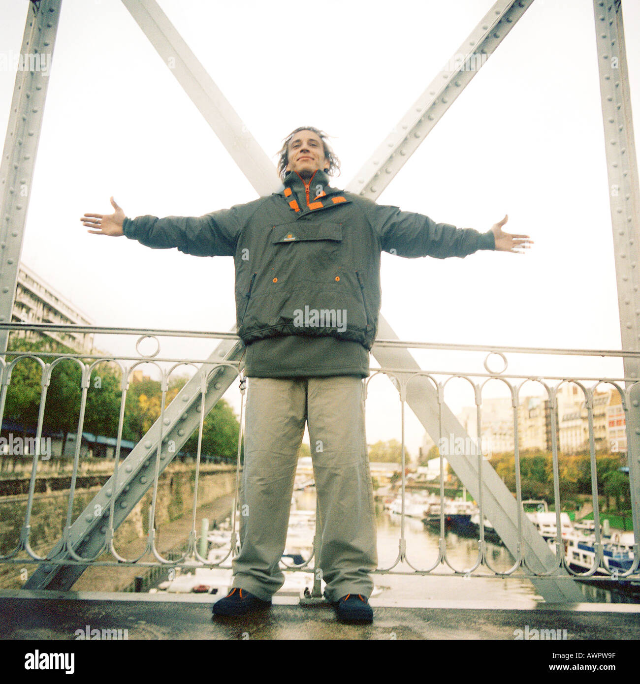 Man standing on bridge wearing winter clothes with arms stretched out ...