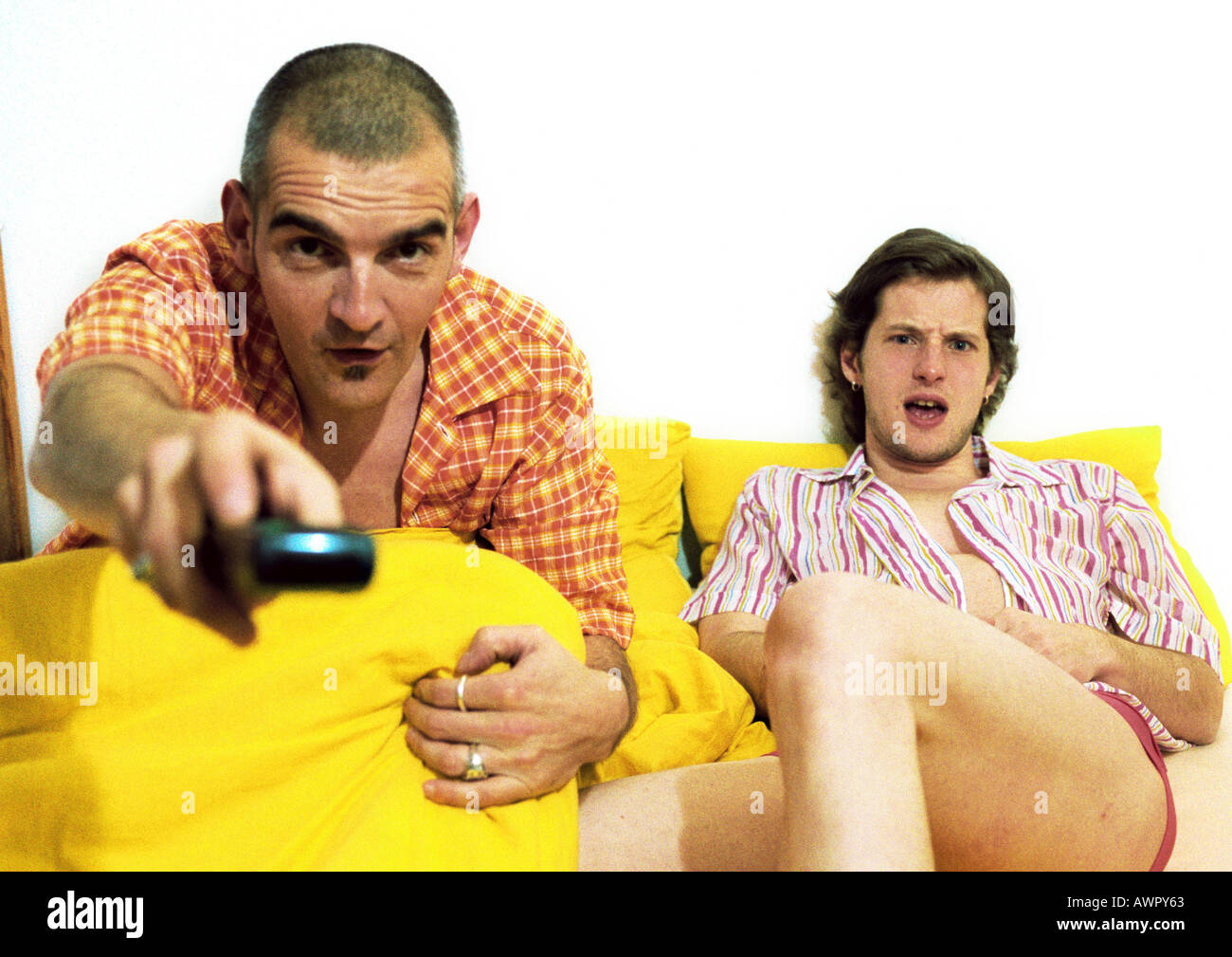 Two men sitting on sofa, one pointing remote control at camera Stock ...