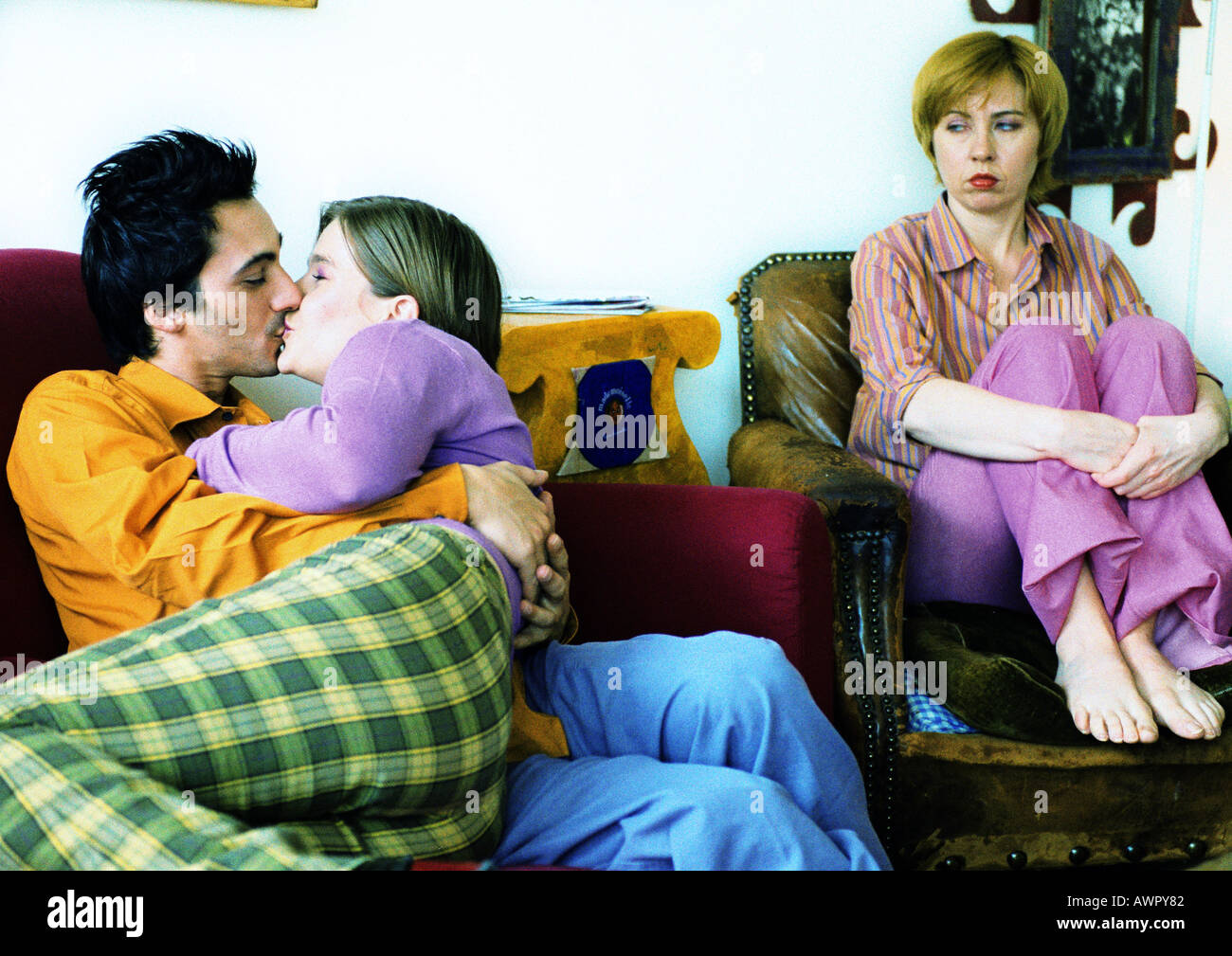 Couple on sofa kissing, second woman sitting in armchair, watching ...