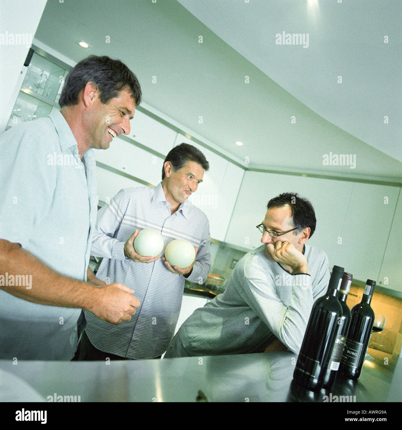 Three men standing in kitchen, one holding melons Stock Photo - Alamy