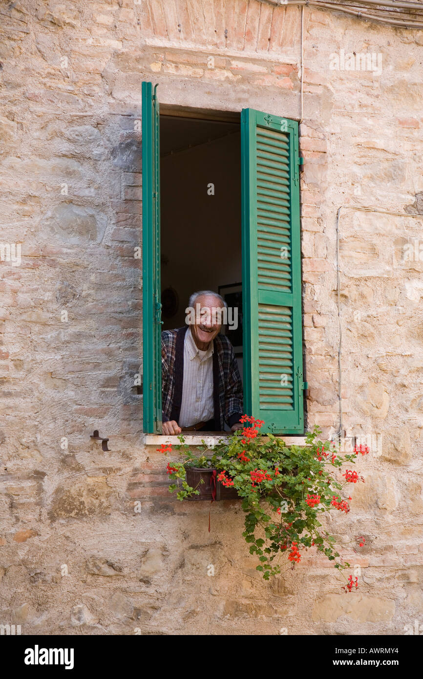 Smiling man looking out window behind partially open green shutters in ...