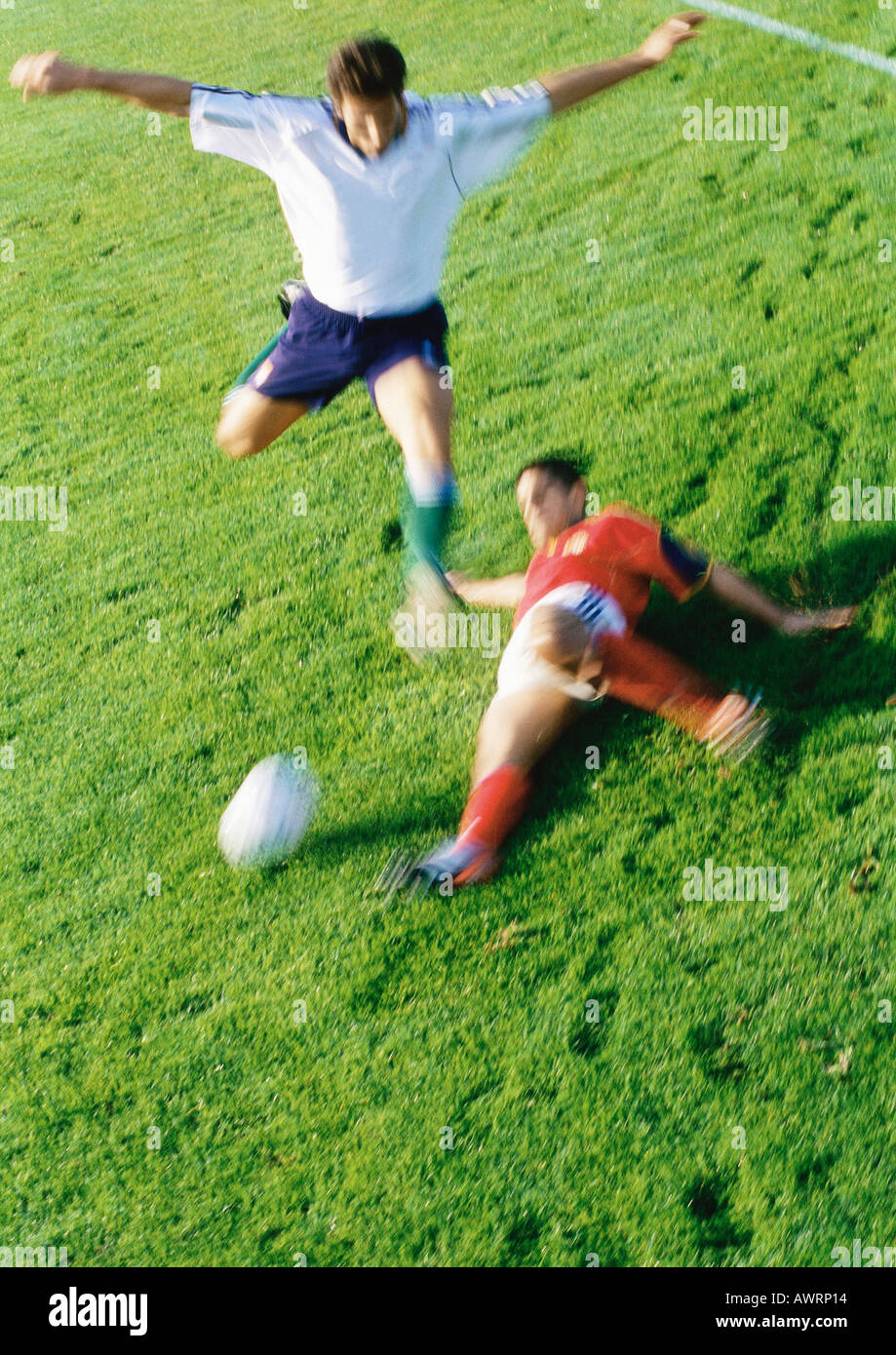 Soccer player reaching for ball, opponent jumping over leg, blurred ...