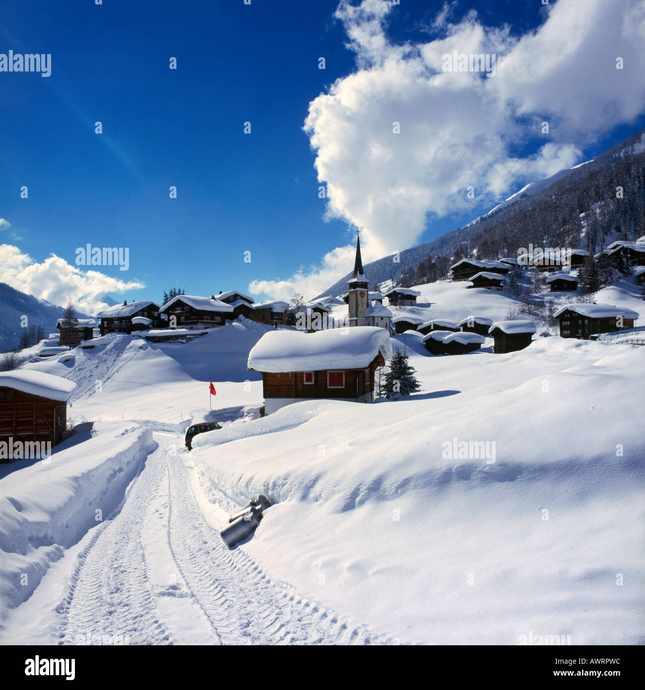 Tyre tracks in heavy winter snow along a road with chalets and church ...