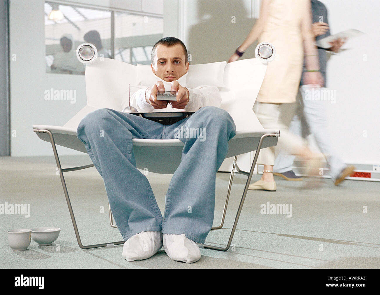 Man in armchair holding remote control, people in background, portrait ...