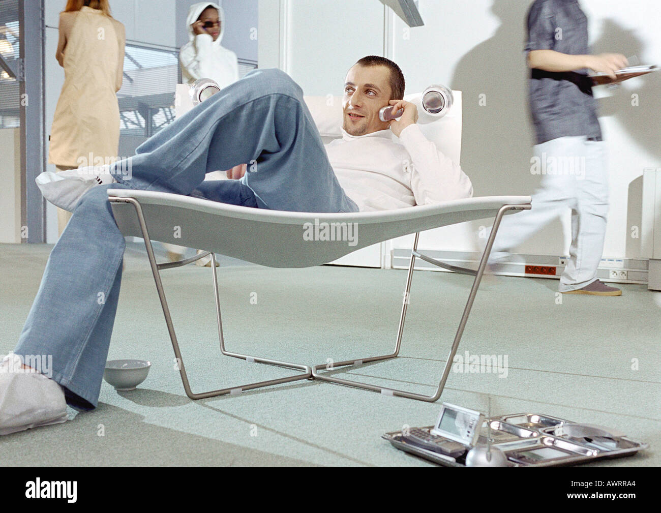 Man sprawling in chair with cell phone while people work Stock Photo ...