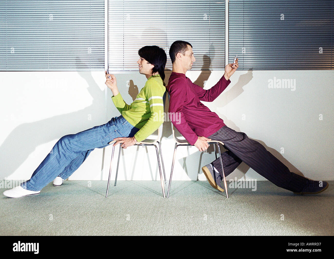 Two men sitting back to back in chairs, using cell phones Stock Photo ...