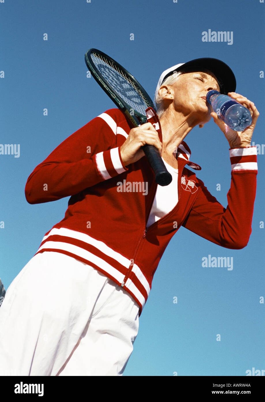 Mature woman holding tennis racket and drinking from bottle of water ...