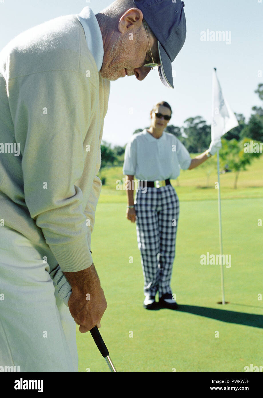 Two mature golfers playing, one putting, the other holding flag Stock ...