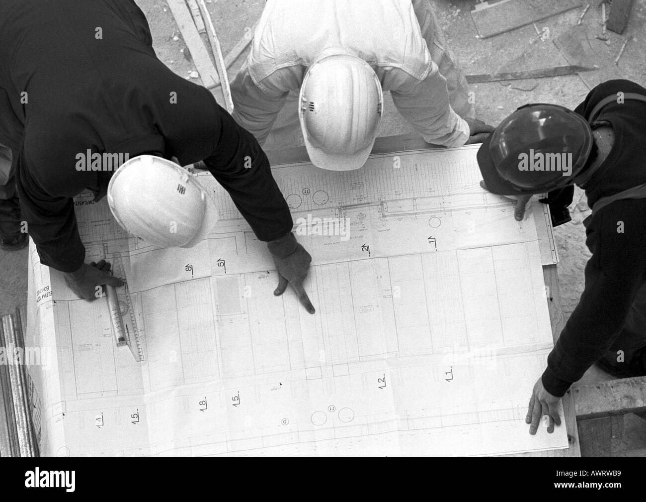 Three people with hard hats, examining blueprint, elevated view, b&w ...