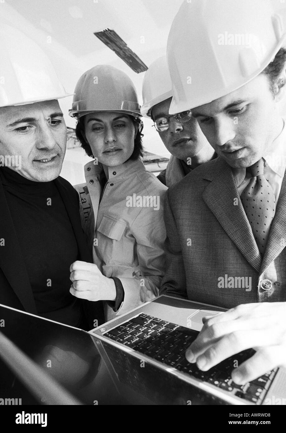 Four people wearing hard hats, one using laptop computer, b&w Stock ...
