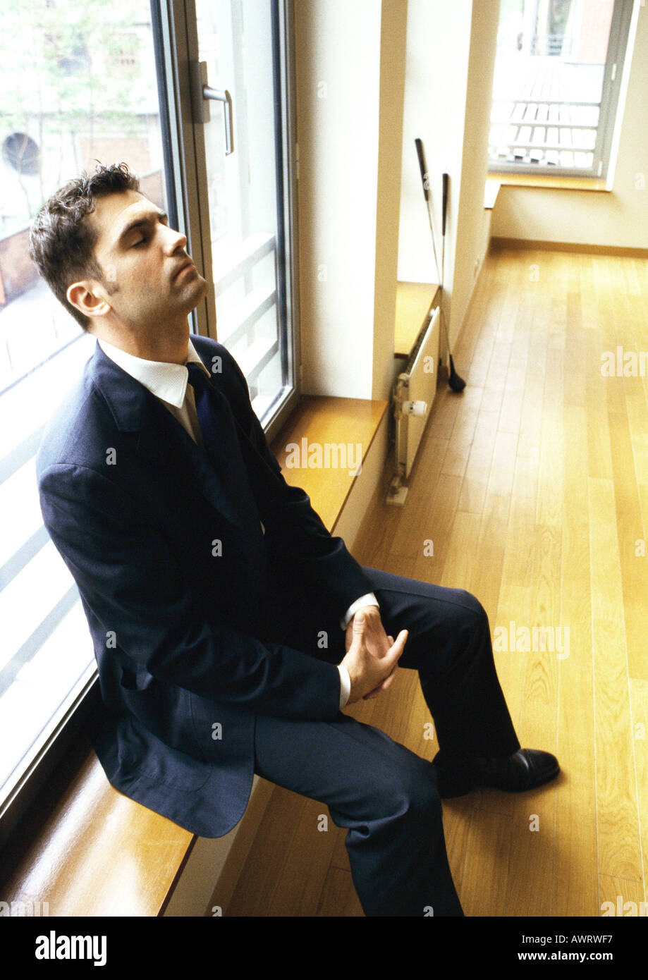Man sitting against window with head back and eyes closed Stock Photo ...
