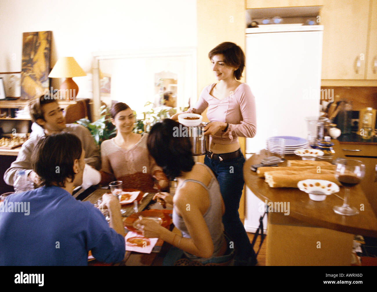 Four people sitting at table, woman bringing dish Stock Photo - Alamy