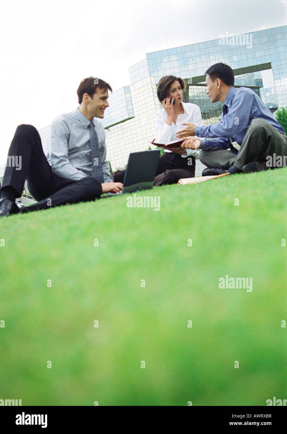 Three people sitting on grass, building in background Stock Photo - Alamy