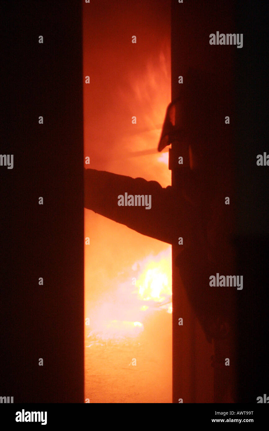 A firefighter inside a burning home opening a door to a room that is on ...