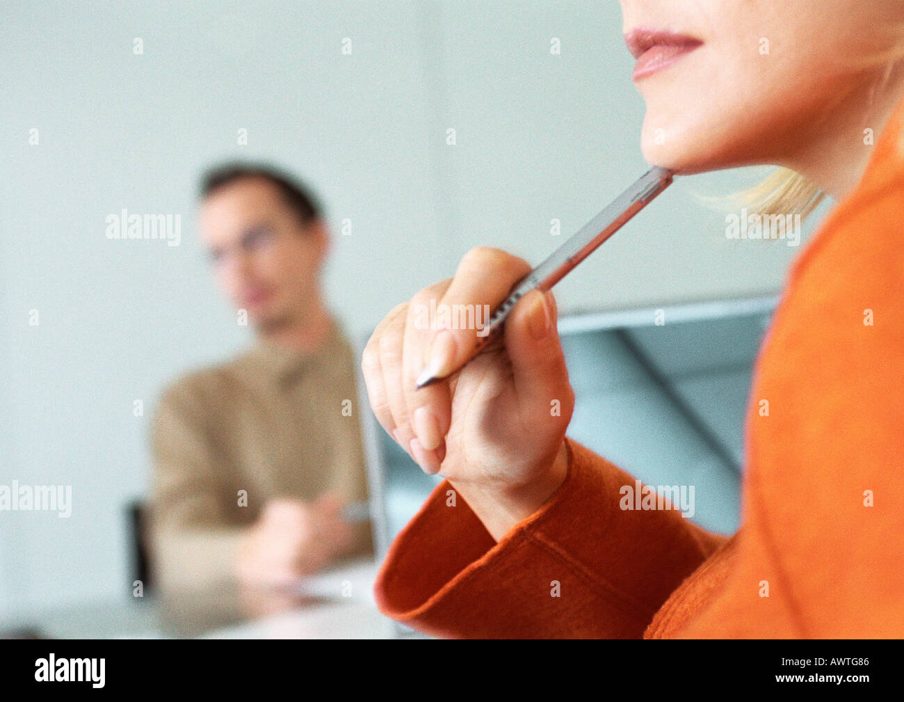 Businesswoman listening holding pen to her chin, man in background ...