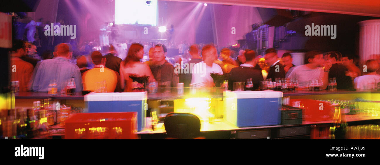 Bar counter, with crowd of people and concert in background, blurred ...