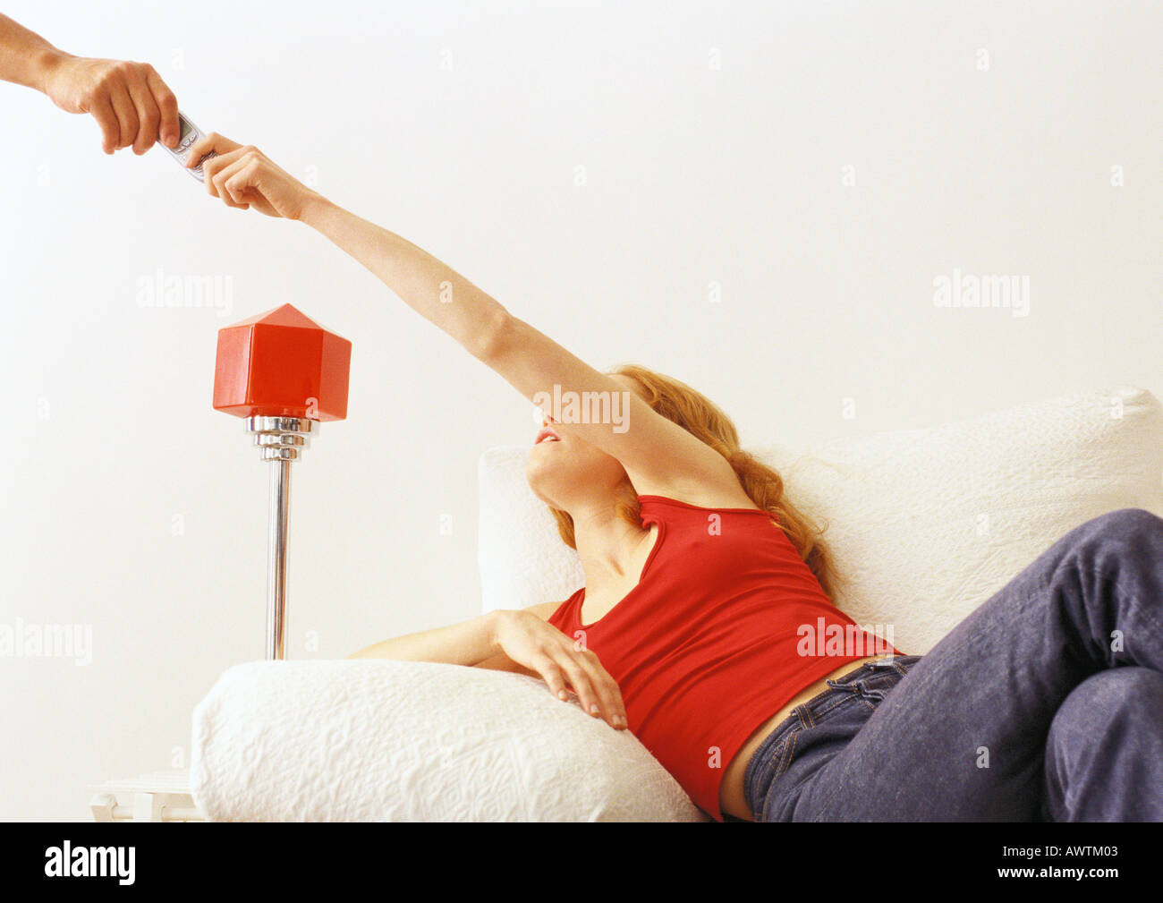 Woman on couch handing remote to someone Stock Photo - Alamy