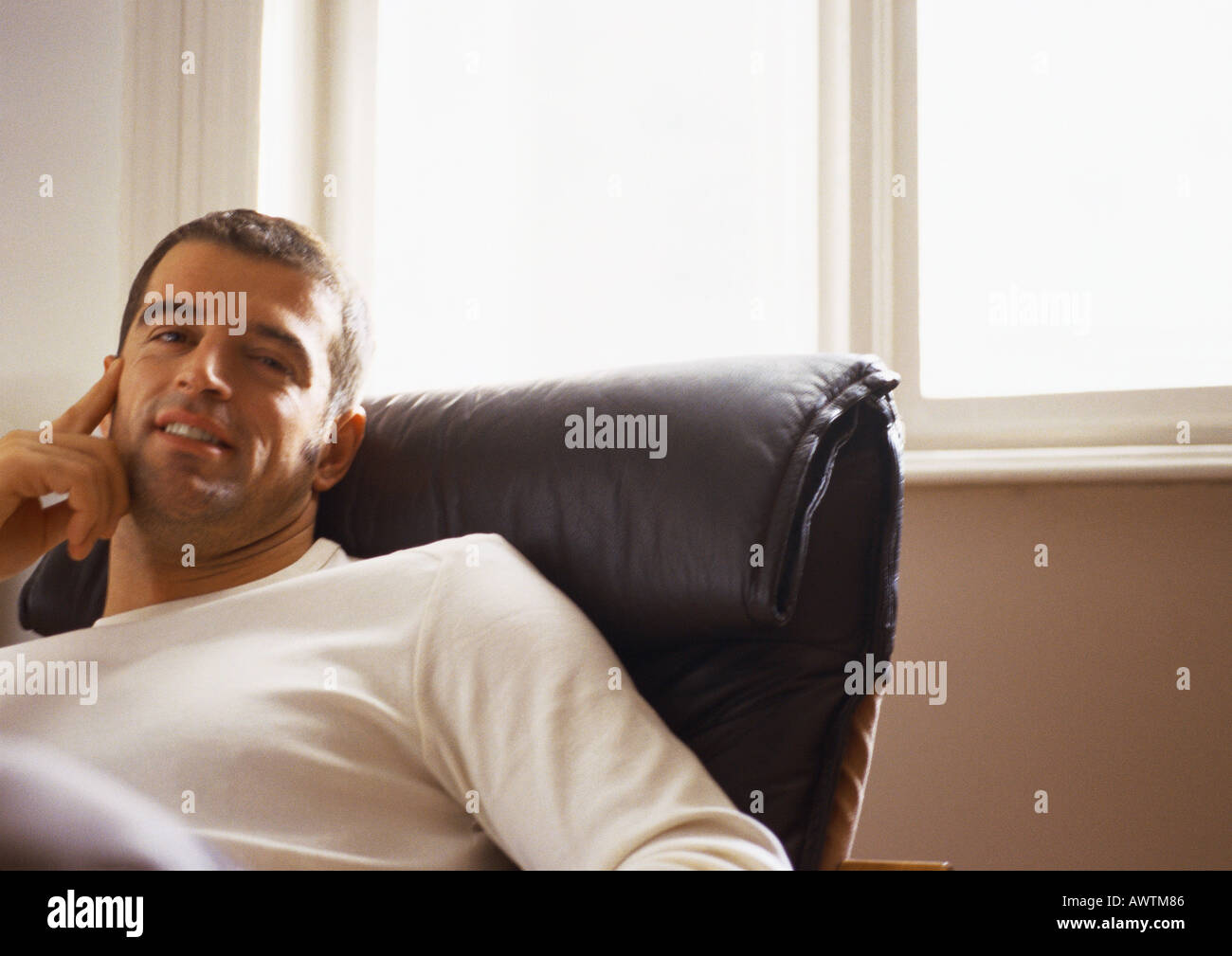 Man sitting in chair, hand to face Stock Photo - Alamy