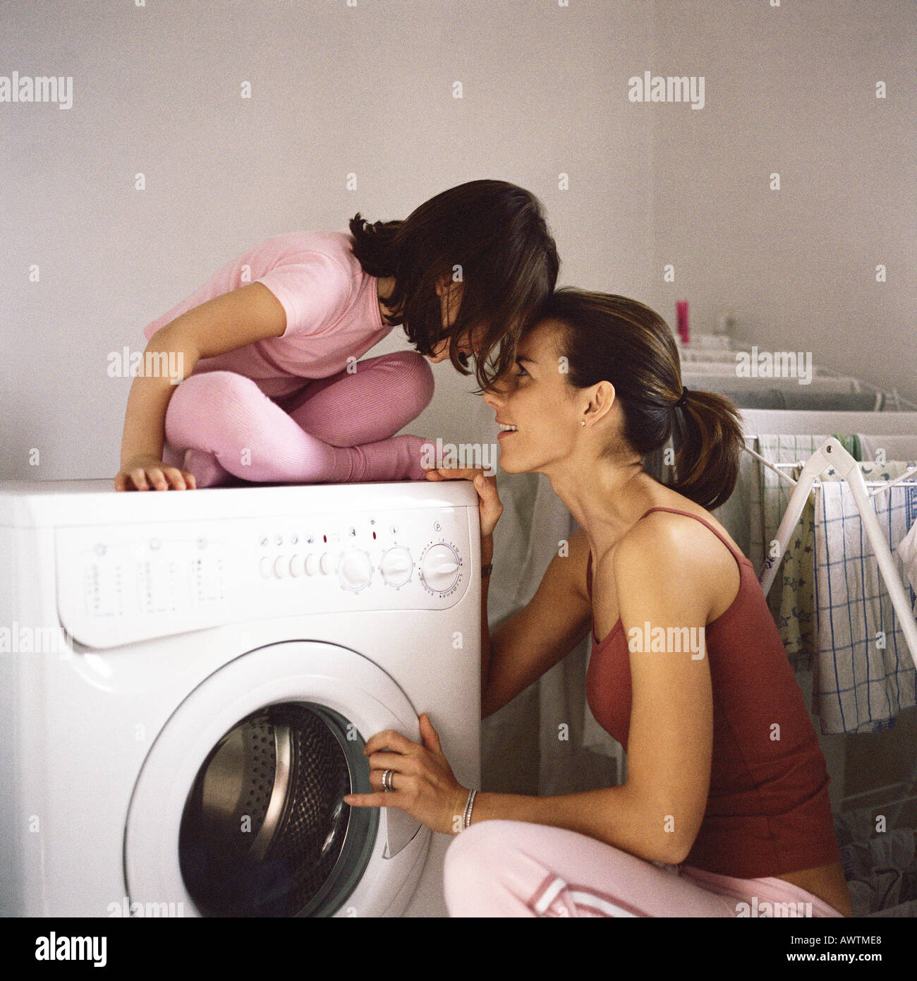 Daughter sitting on washing machine, head to head with mother Stock ...