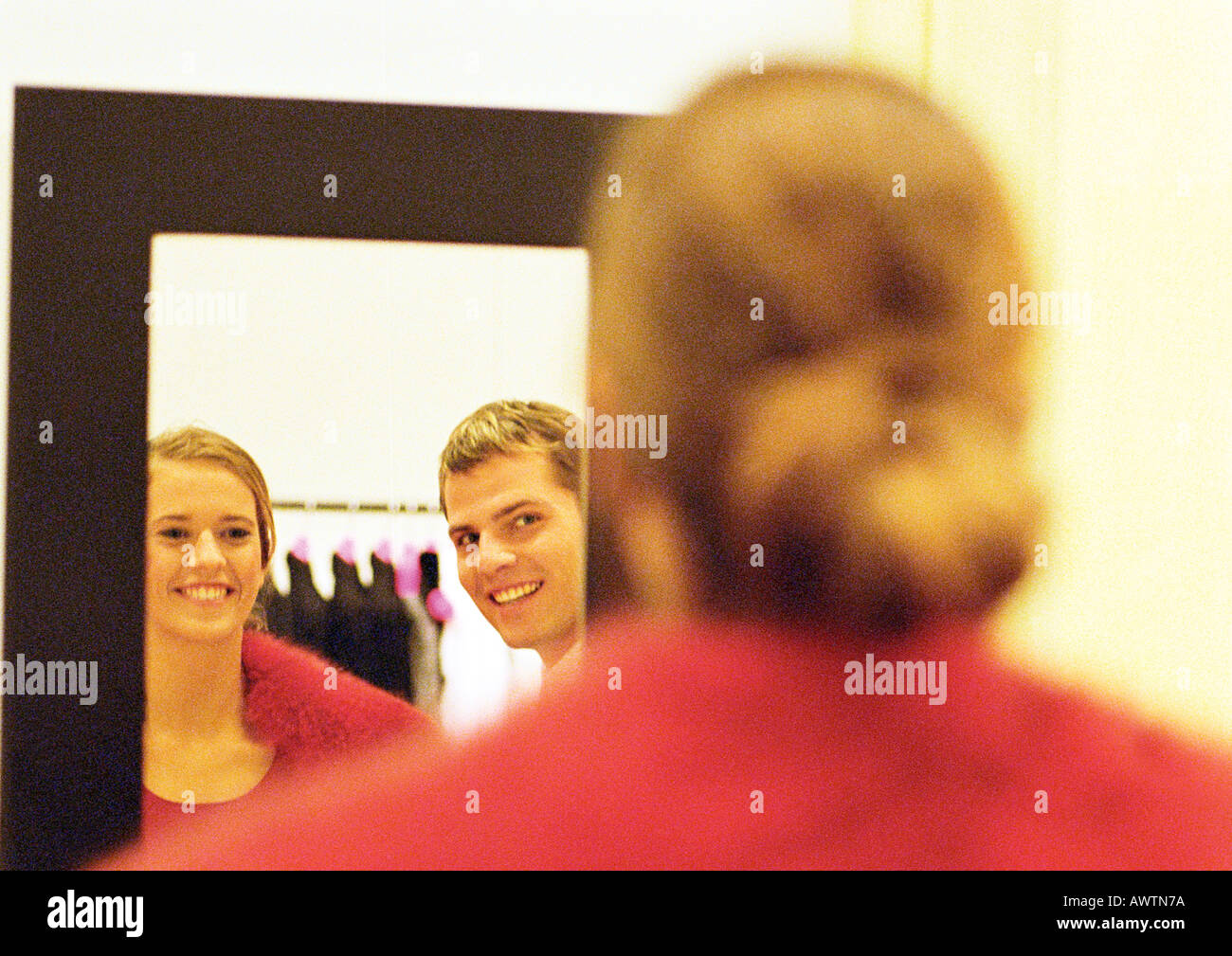 Woman trying on coat, smiling at boyfriend in mirror Stock Photo - Alamy