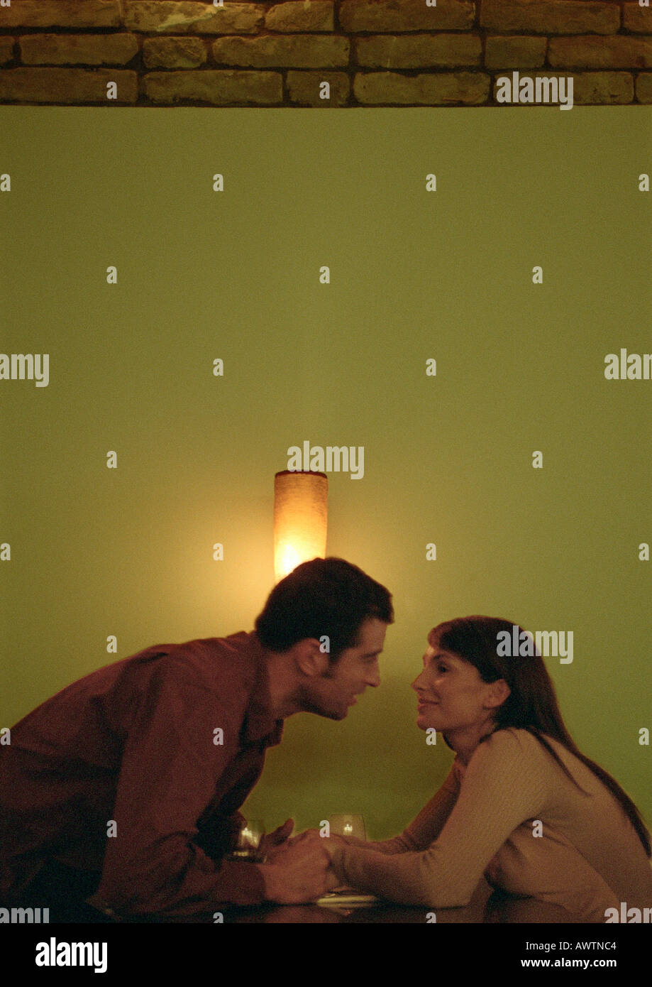 Man holding woman's hands, leaning across table to kiss her Stock Photo ...