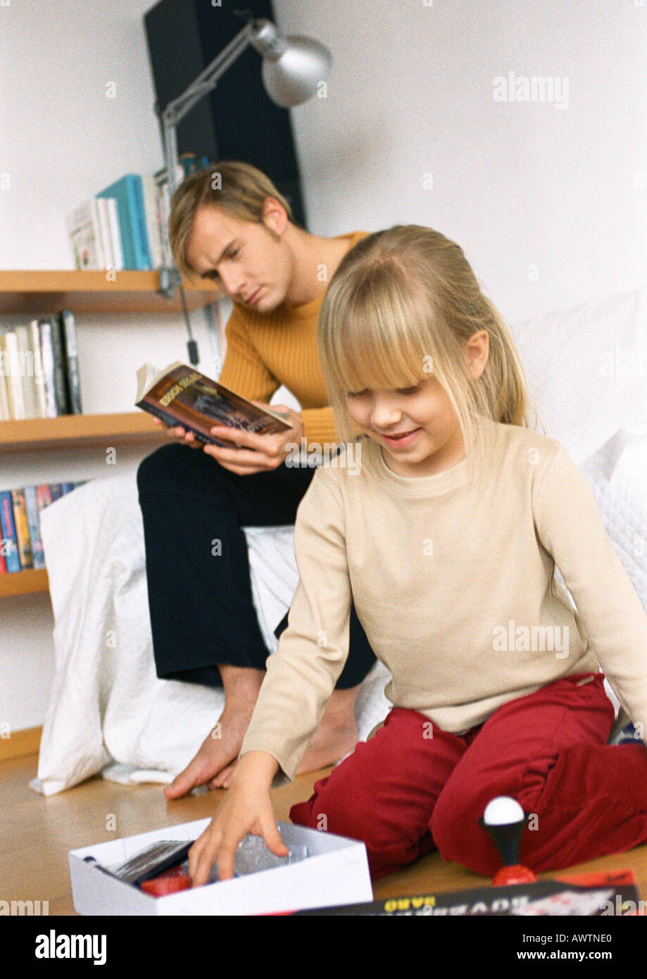 Daughter looking at objects in box, father reading nearby Stock Photo ...