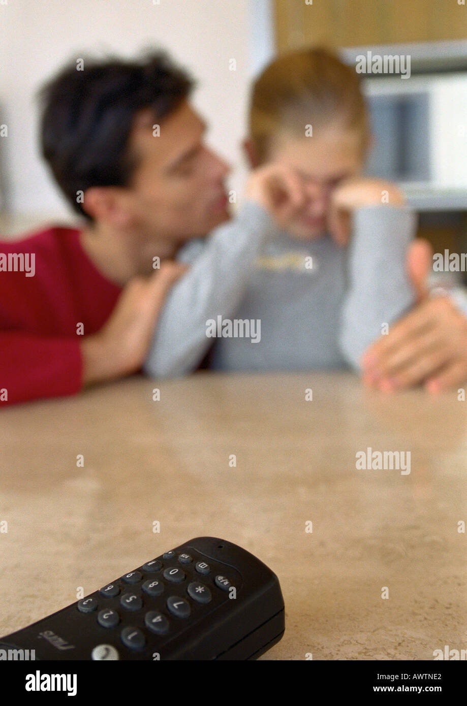 Remote control on table, father and daughter in background, blurred ...