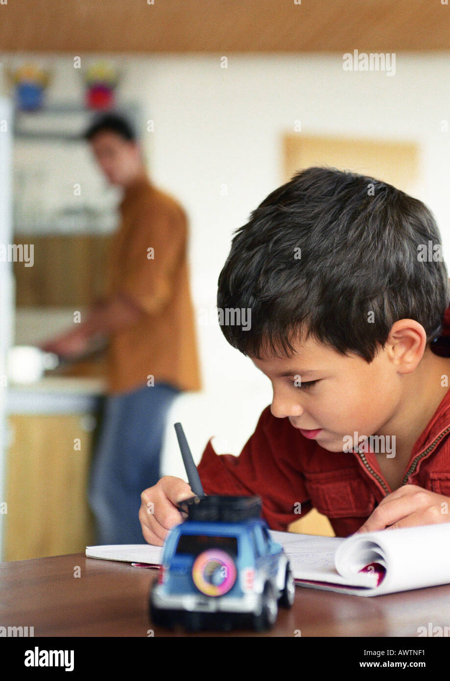 Son writing, father in background blurred Stock Photo - Alamy