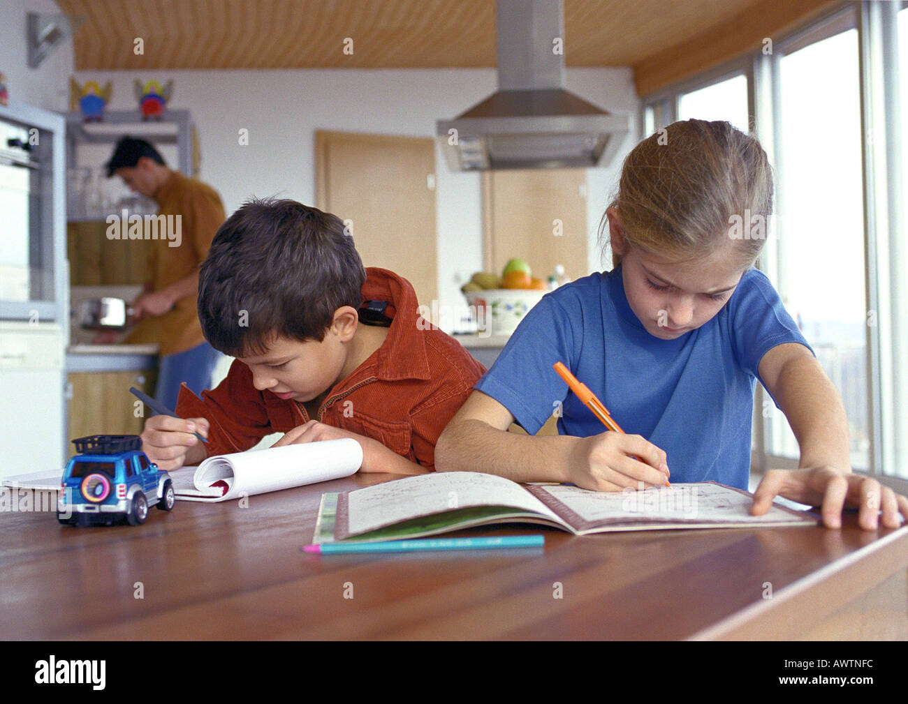Son and daughter writing at table, father in background cooking ...
