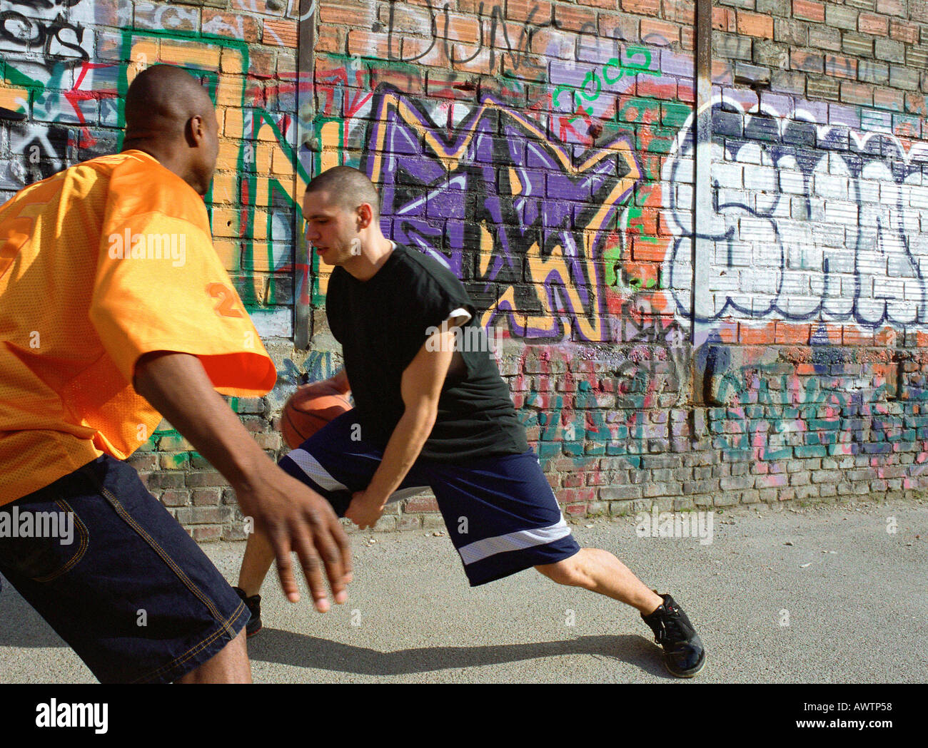 Man dribbling basketball, opponent blocking, next to graffitied wall ...