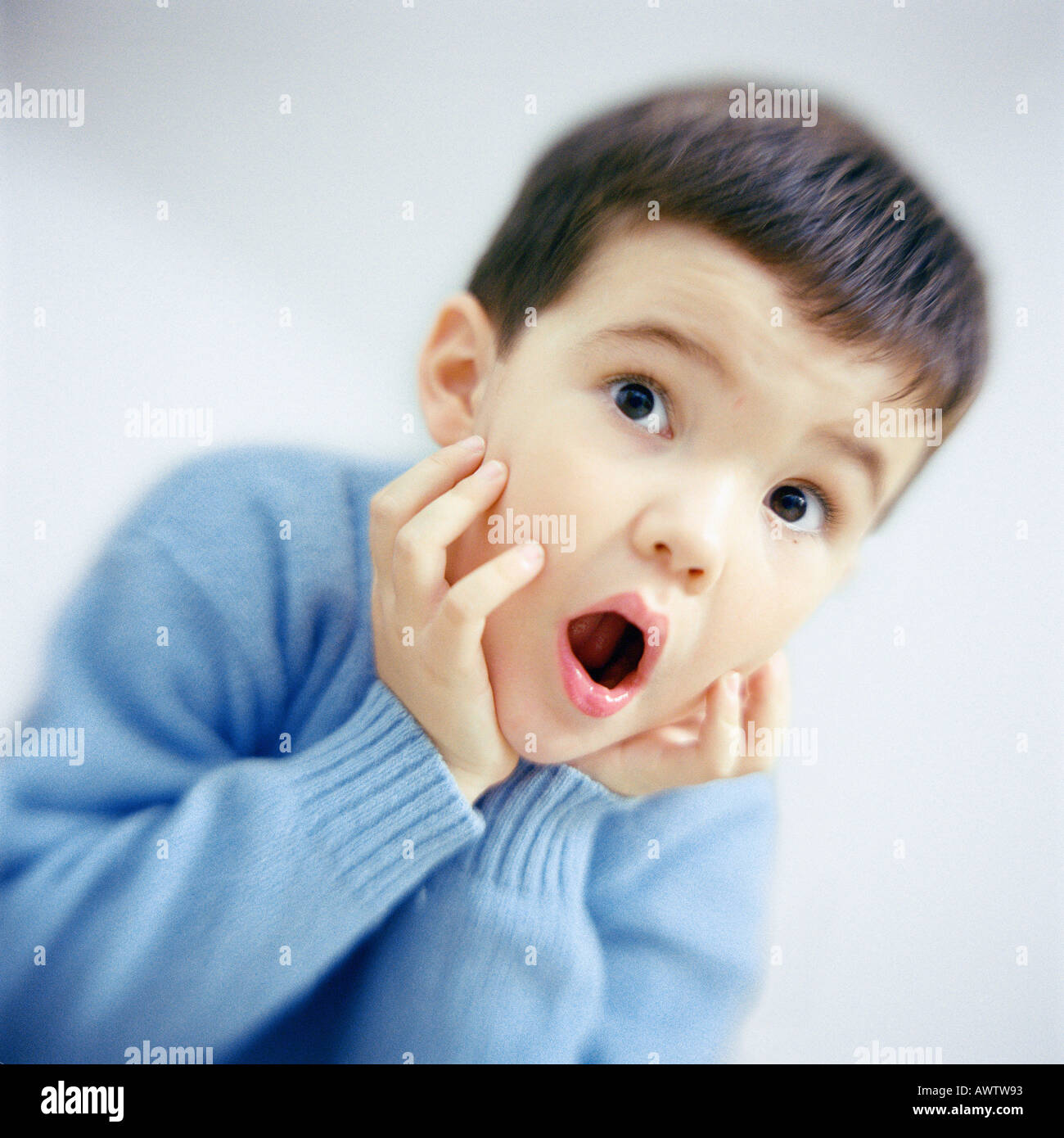 Boy, hand on cheeks, eyebrows raised and open mouth, head and shoulders ...