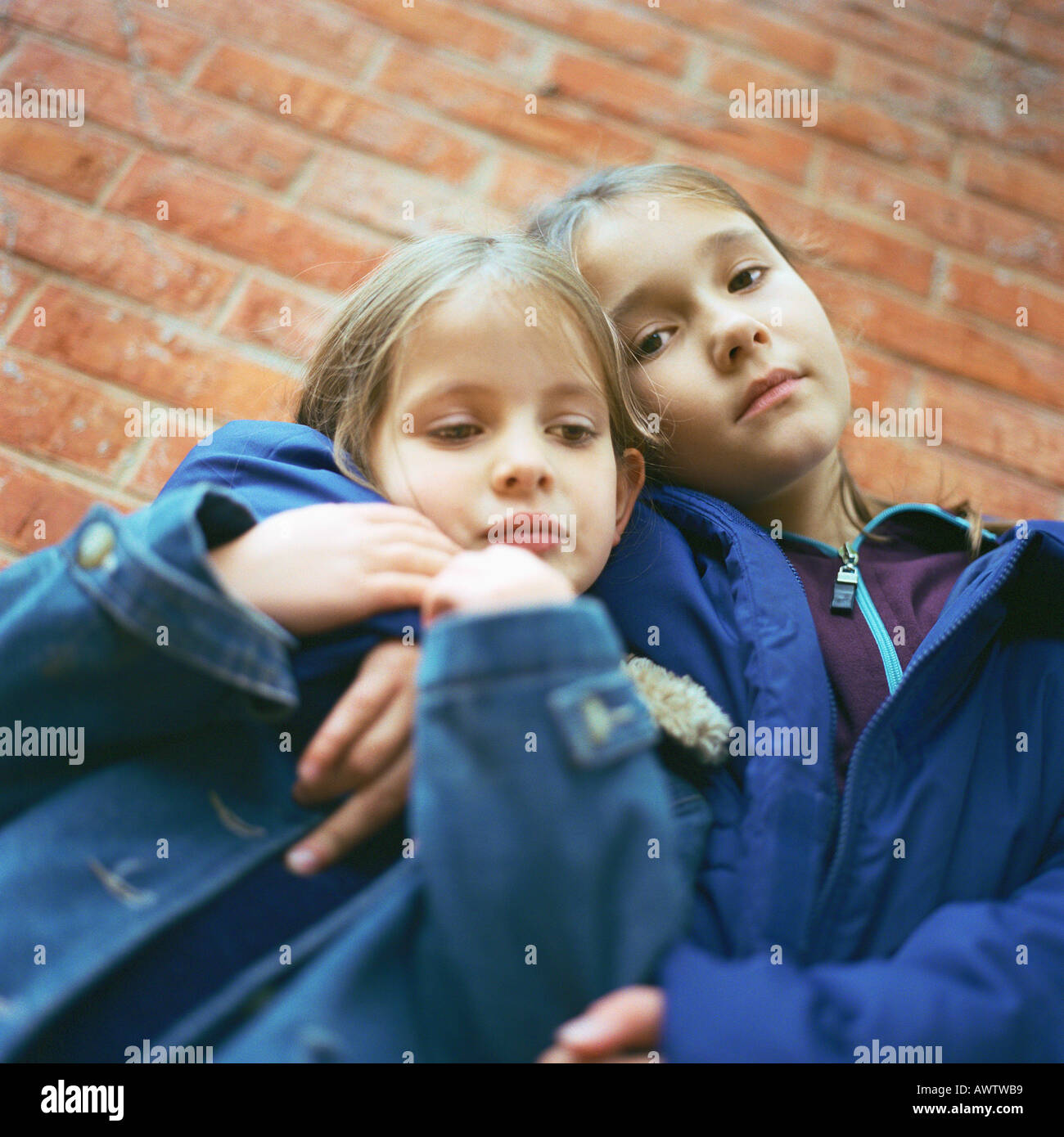 Two girls hugging, brick wall in background, low angle view Stock Photo ...