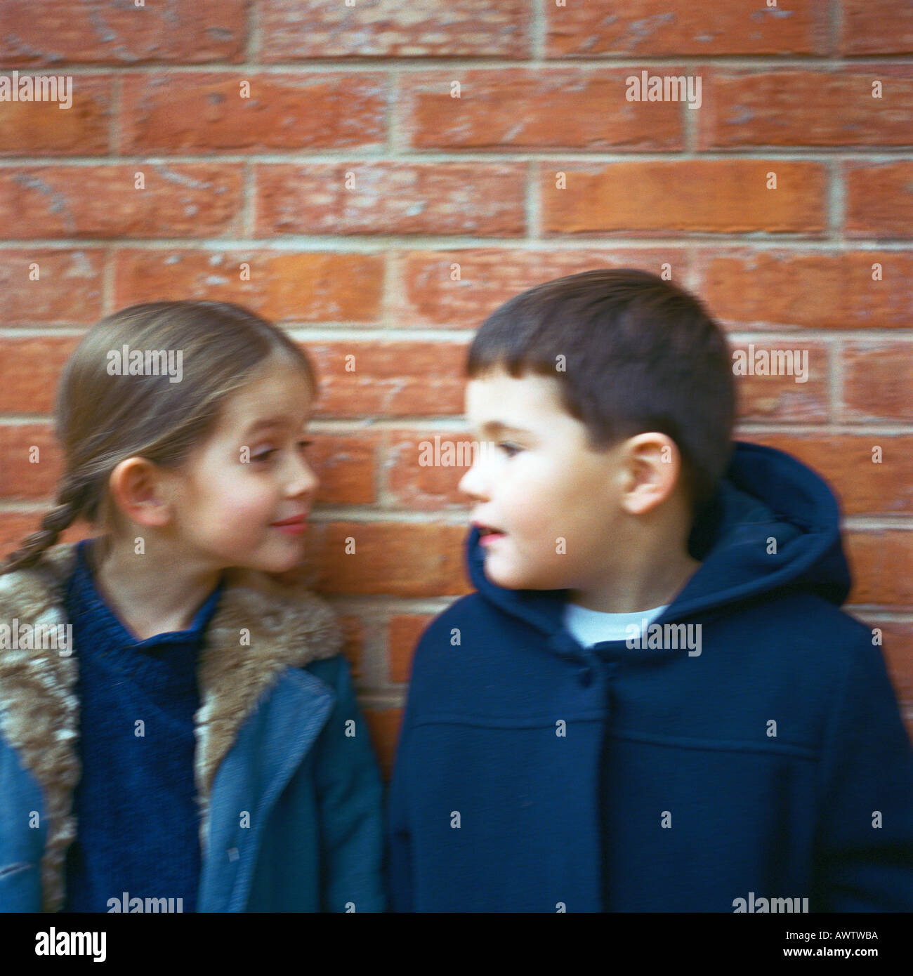 Boy and girl standing in front of brick wall, staring eachother down ...