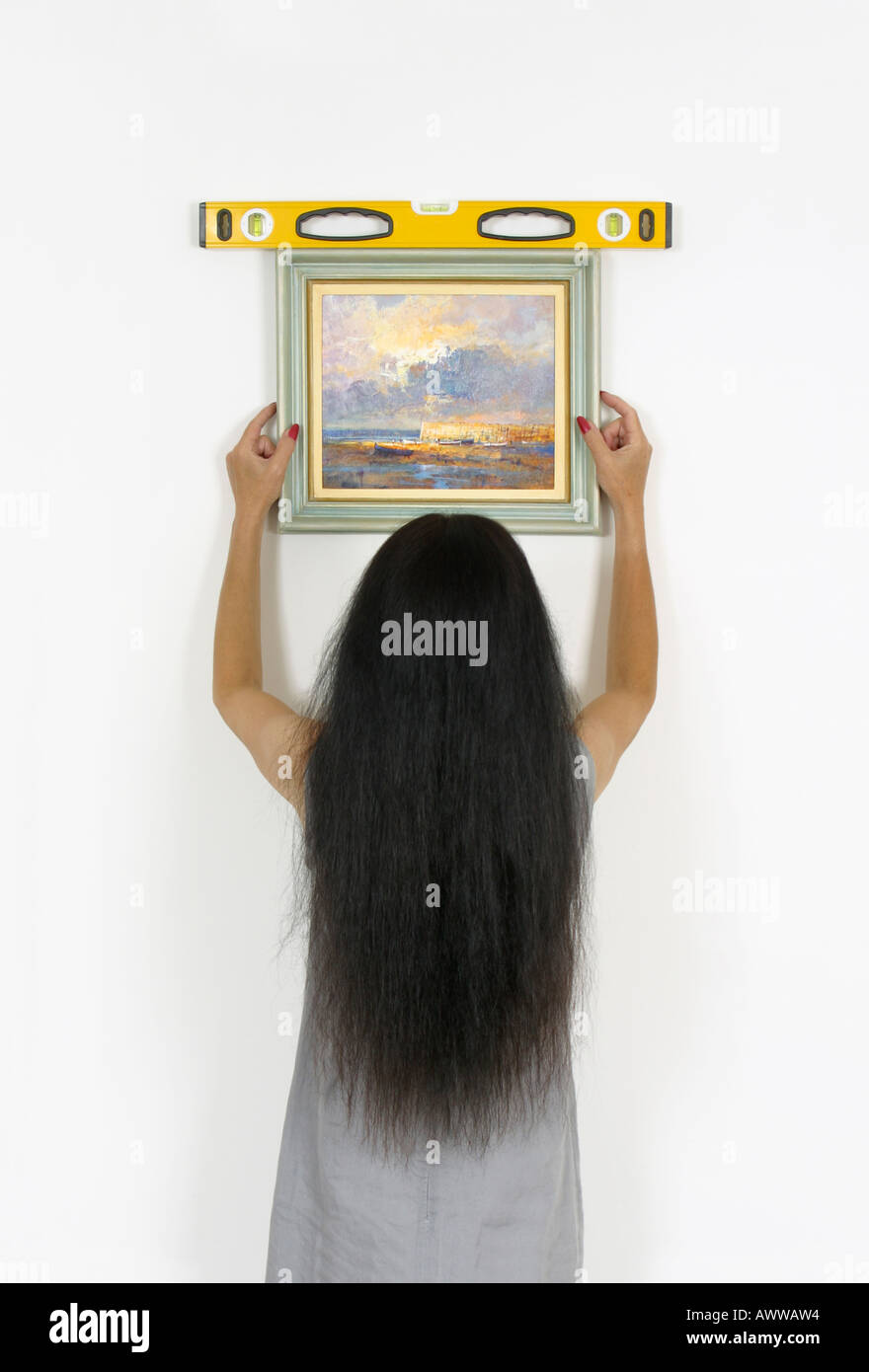 Long haired woman using spirit level to hang picture on wall Stock ...